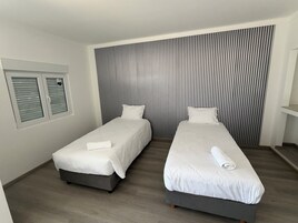 Quarto de hotel com duas camas de solteiro, uma janela com persianas e parede listrada.