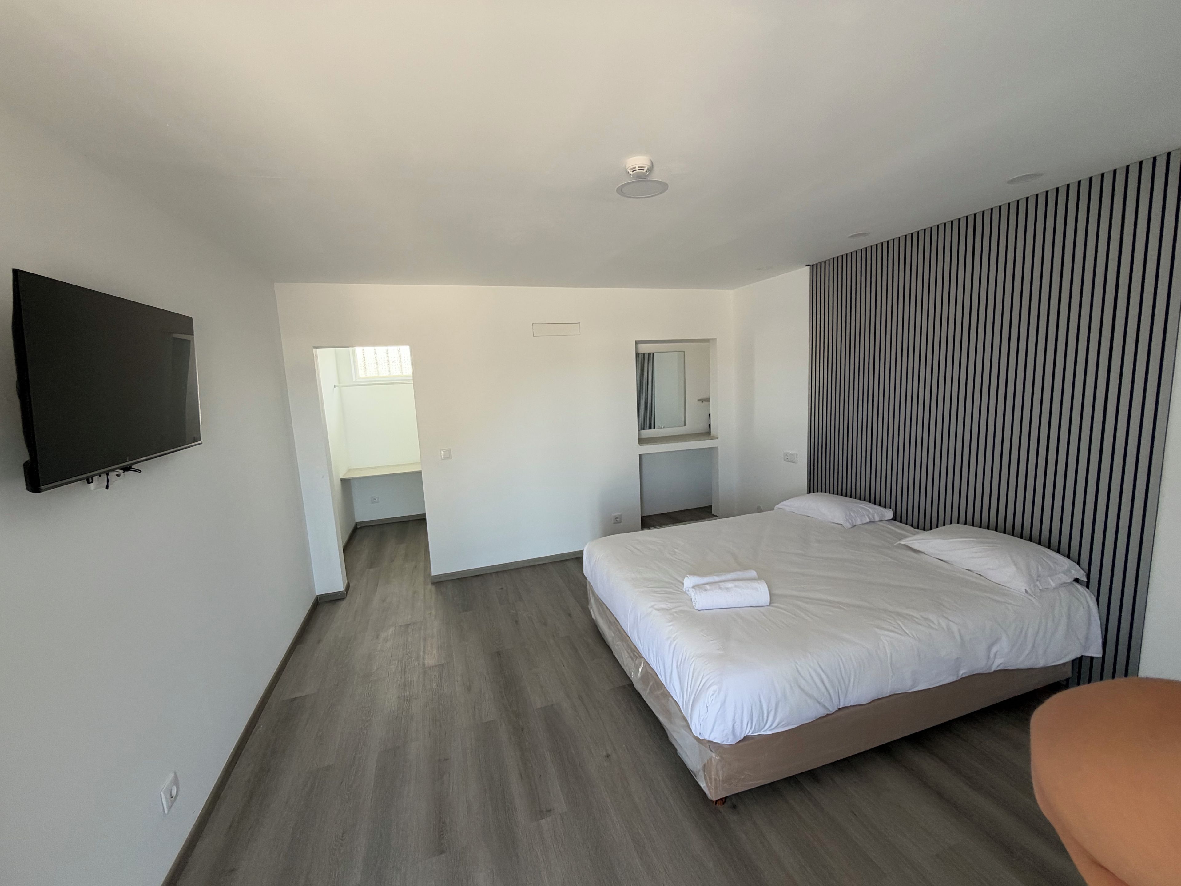 Quarto de hotel moderno com uma cama grande, televisão de tela plana na parede, um pequeno espaço de estar e banheiro com espelho.