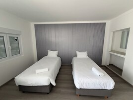 Quarto de hotel com duas camas de solteiro, janela com persianas, espelho e parede listrada.