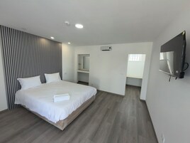 Quarto de hotel moderno com uma cama grande, televisão de tela plana na parede e um closet espaçoso.