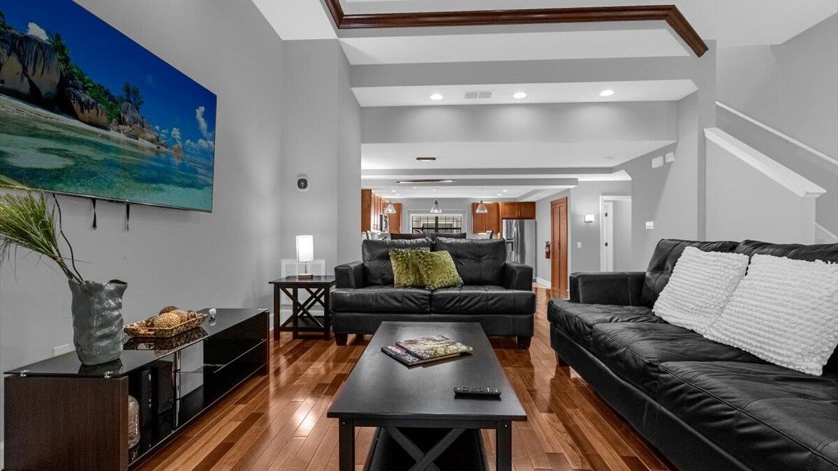 Uma sala de estar moderna com um sofá de couro preto, uma mesa de centro e uma TV de tela plana fixada na parede.