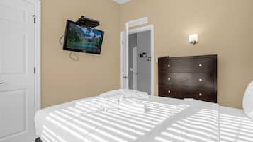 Quarto de hotel com cama, televisão presa à parede, penteadeira e porta que dá para outro espaço.