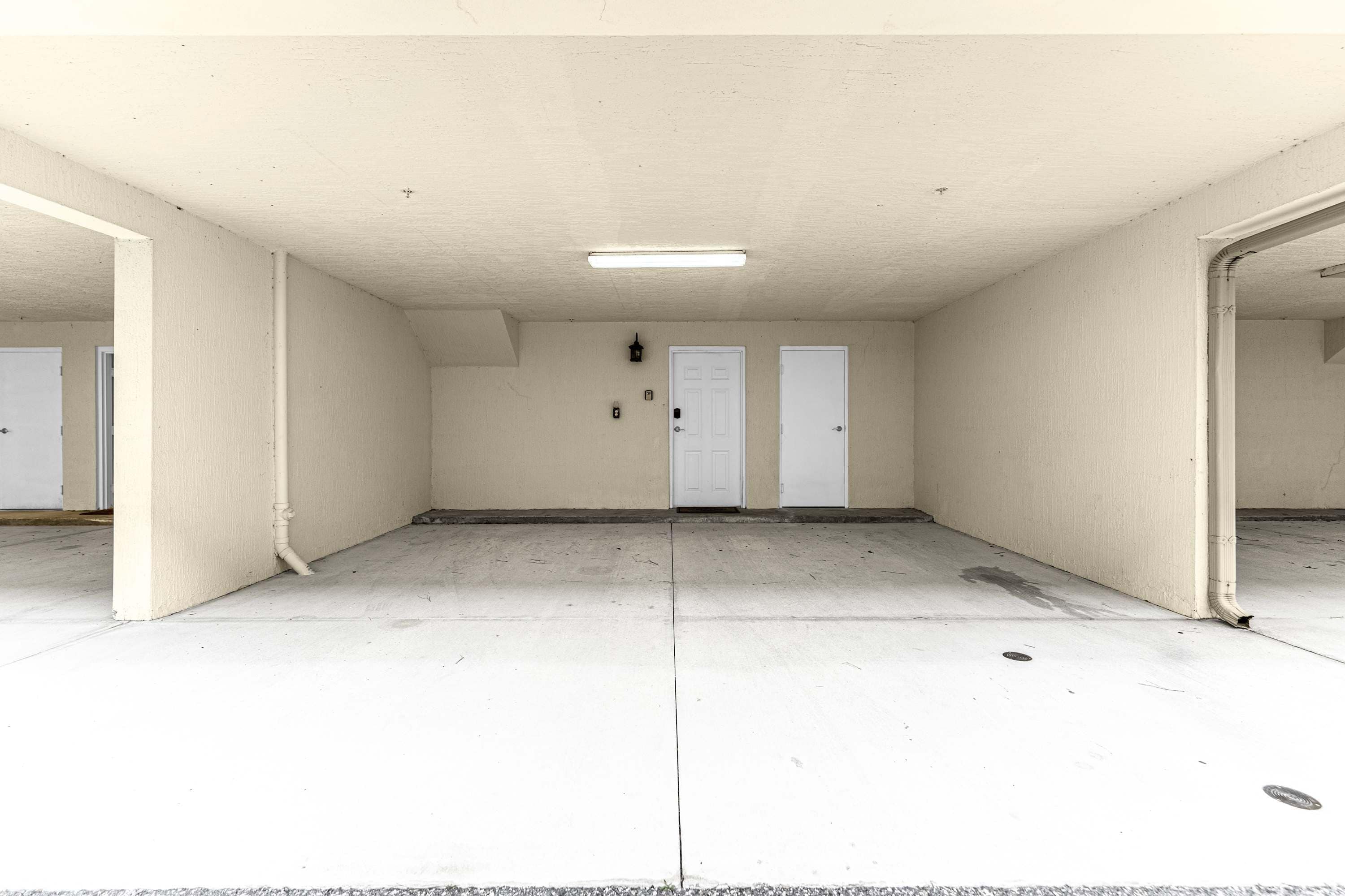 Quarto vazio com paredes e teto brancos e chão de concreto. Há duas portas brancas e um aparelho de luz na parede.