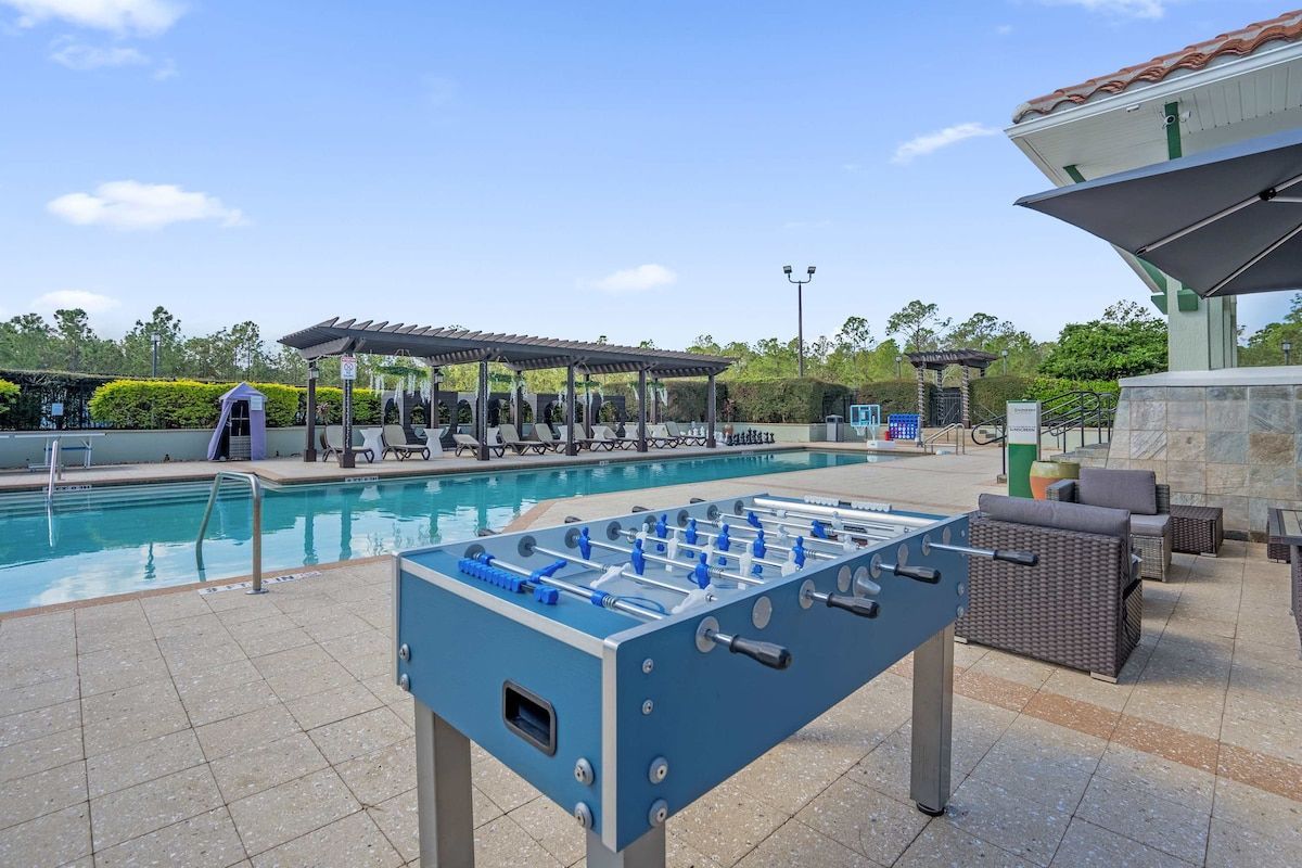 Uma área de piscina com mesa de pebolim, cadeiras de estar e área de estar coberta.