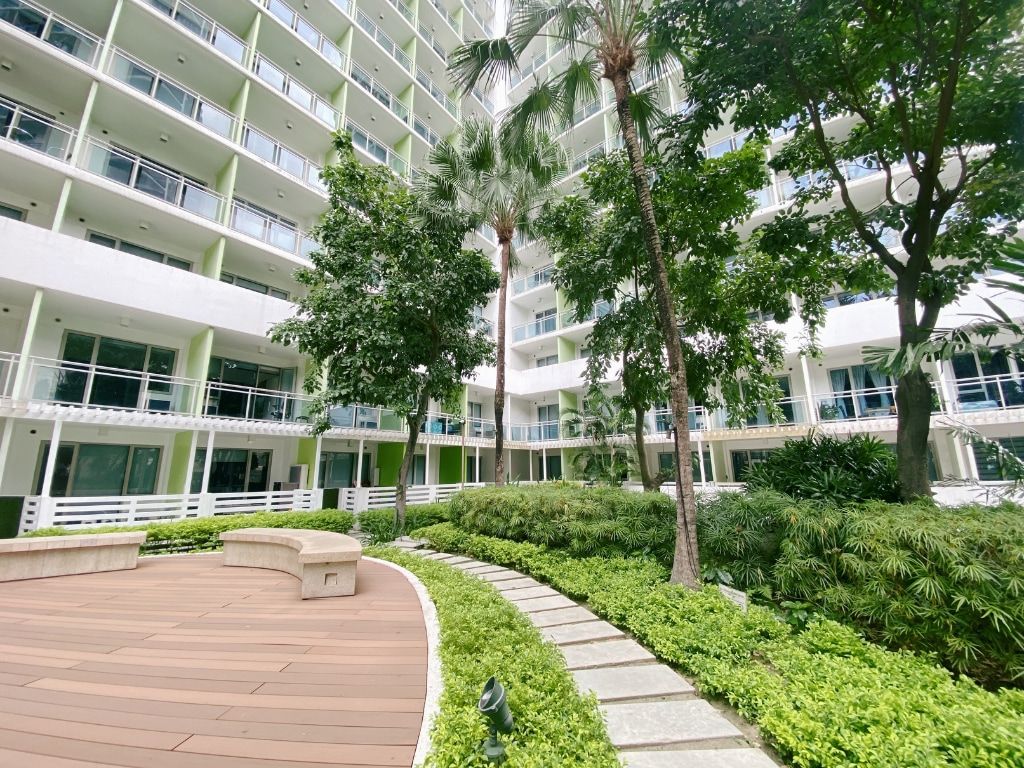 Hotel com vários andares e pátio central com um caminho curvo, palmeiras e diversos arbustos.