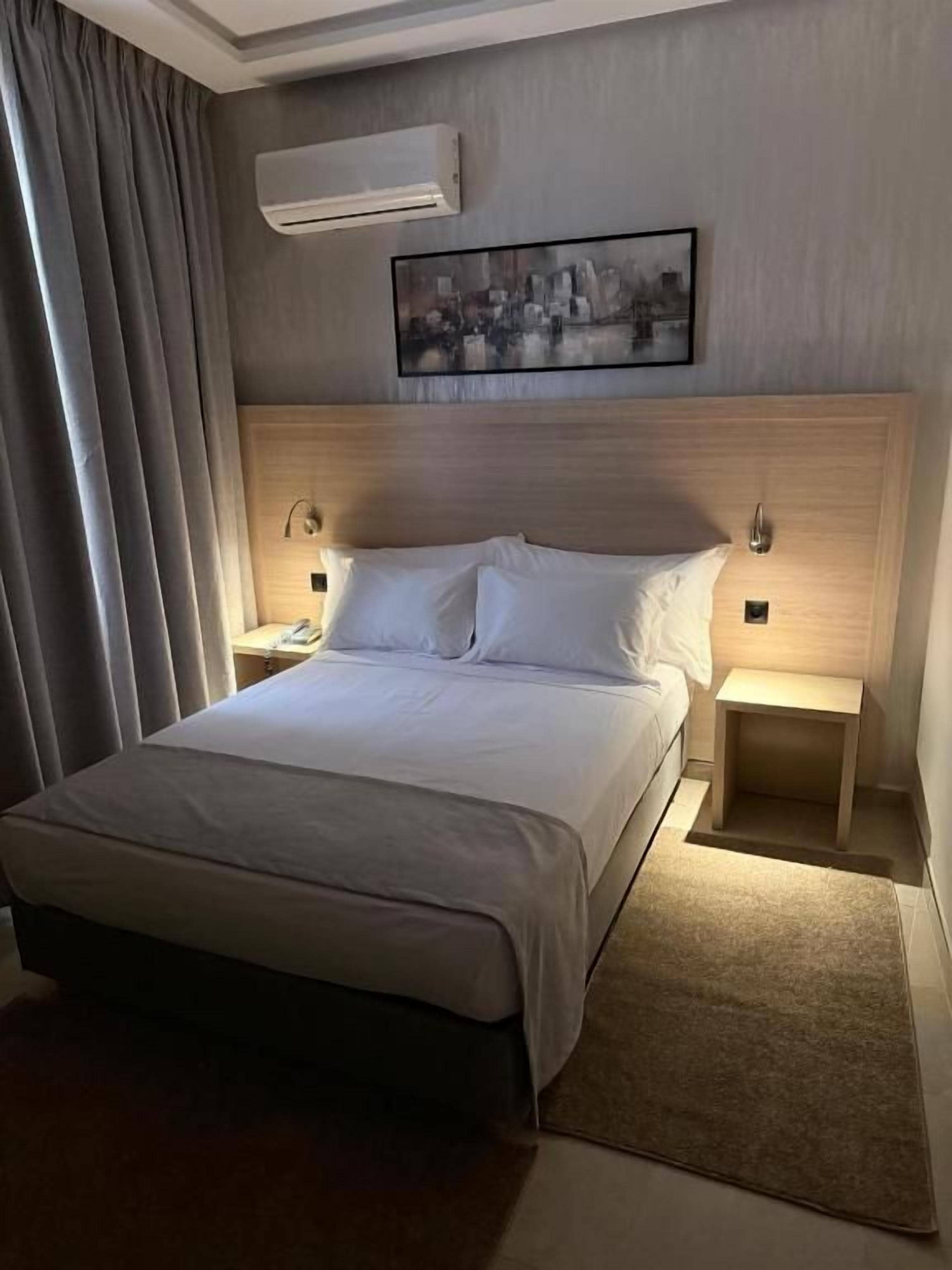 Quarto de hotel com cama, mesas de cabeceira, ar condicionado e um quadro na parede.