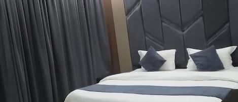 Quarto de hotel com cama, cortinas, ar condicionado e uma escrivaninha.