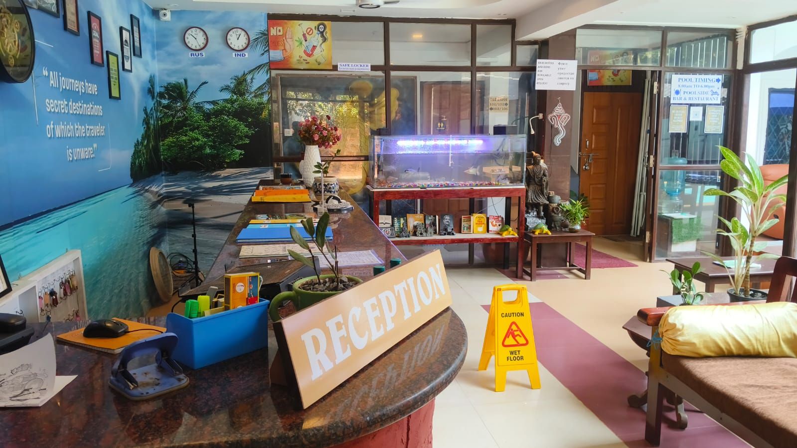 Uma área de recepção com placa, relógio, armário de segurança e aviso de piso molhado.