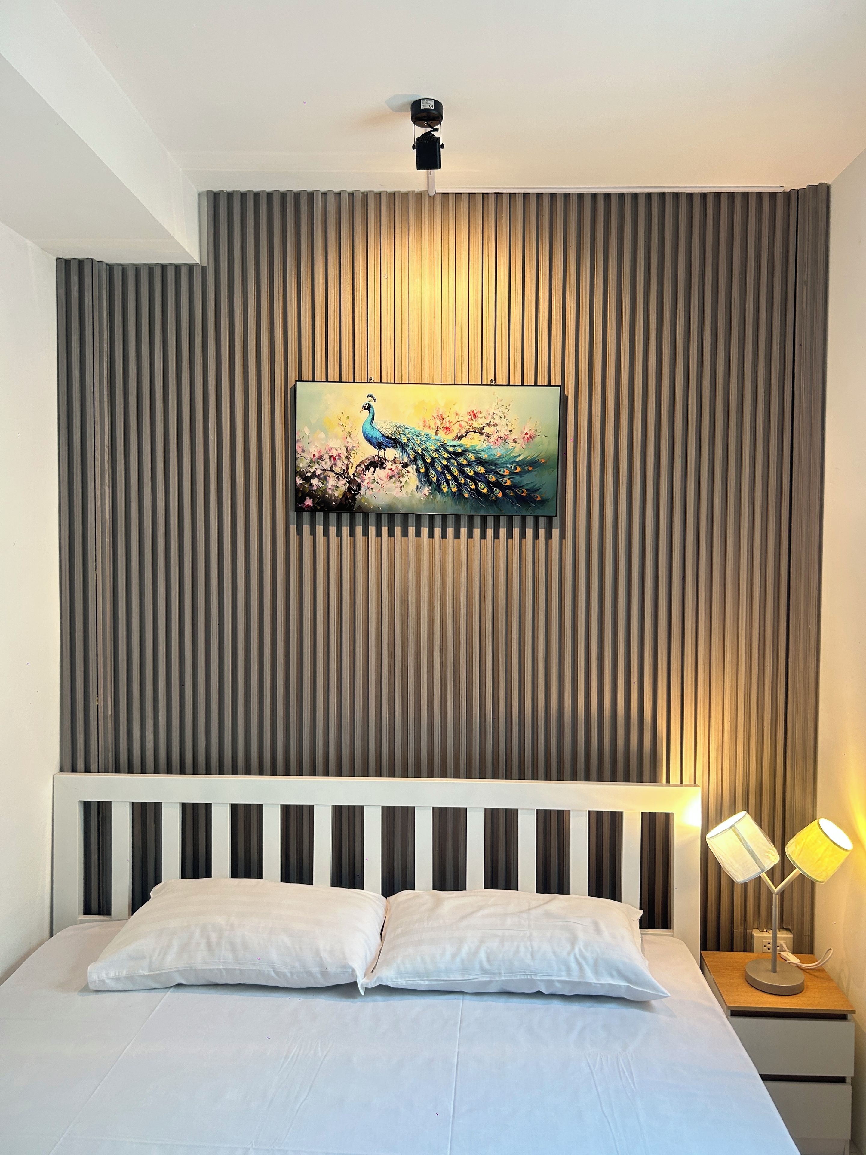 Quarto com cama, pintura de um pavão pendurada na parede e mesa de cabeceira com abajur.