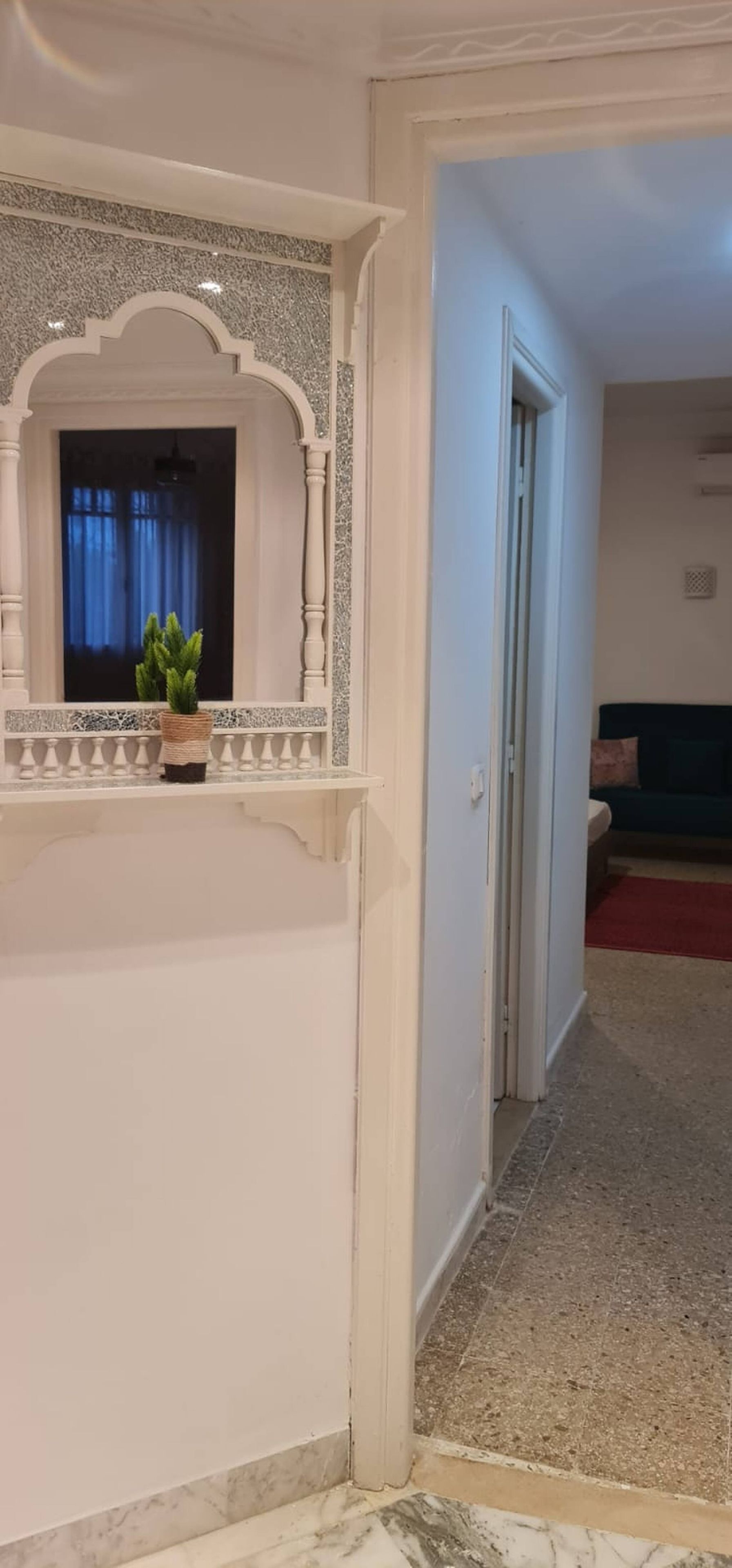 Um corredor com parede branca, piso de mármore e uma porta que dá para outro cômodo.