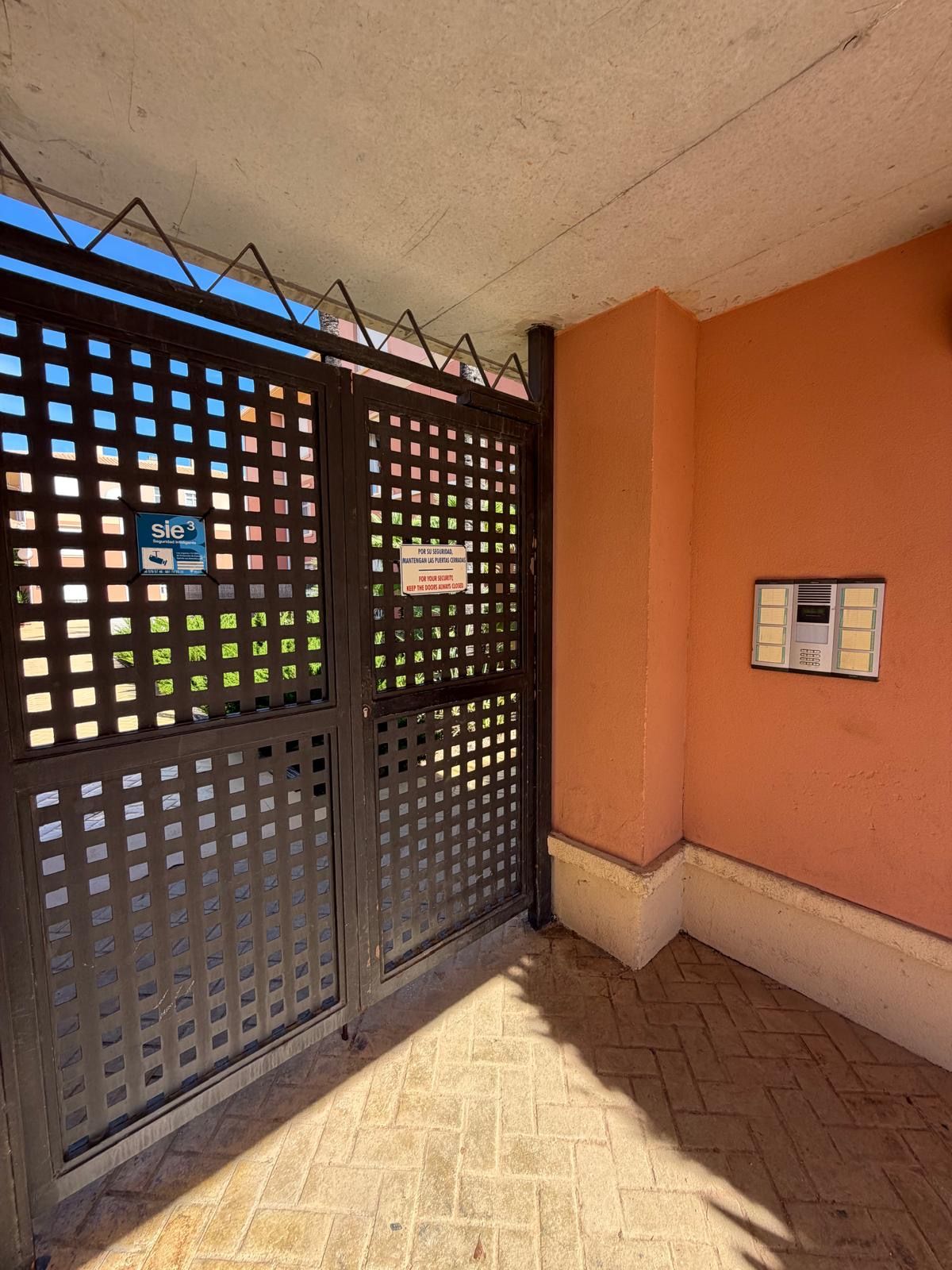 Uma entrada protegida por grades, um letreiro, piso de azulejos e uma parede com uma pequena janela.