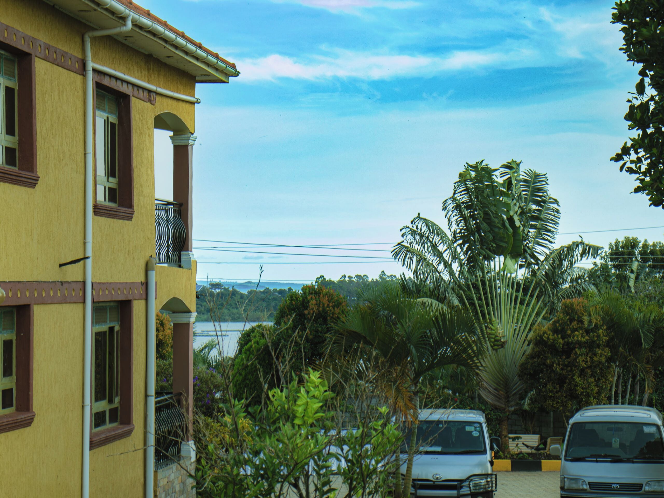 Edifício amarelo com varanda, um carro estacionado e uma palmeira ao primeiro plano.