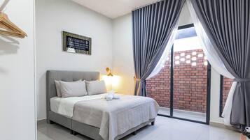 Quarto com cama, luminária na parede e vista para uma parede de tijolos através de uma janela com cortinas.