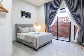 Quarto com cama, luminária na parede e vista para uma parede de tijolos através de uma janela com cortinas.