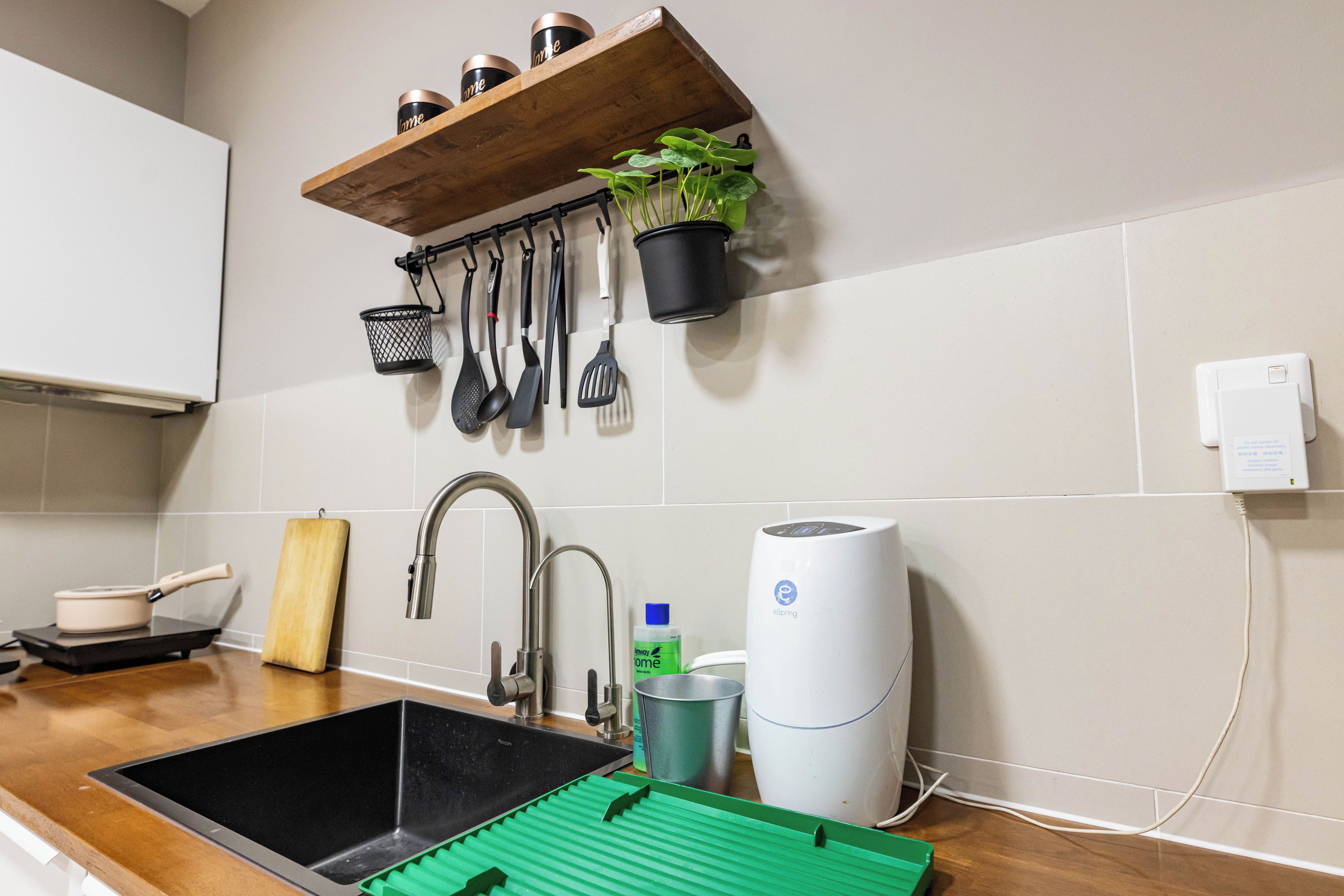 Uma cozinha com pia, torneira, tábua de corte verde, um aparelho eSpring branco e diversos utensílios pendurados na parede.