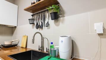 Uma cozinha com pia, torneira, tábua de corte verde, um aparelho eSpring branco e diversos utensílios pendurados na parede.