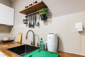 Uma cozinha com pia, torneira, tábua de corte verde, um aparelho eSpring branco e diversos utensílios pendurados na parede.