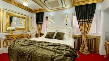 Um quarto luxuoso com uma cama grande, espelhos dourados ornamentados e cortinas elegantes.