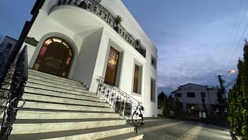 Um edifício com uma entrada imponente, uma escadaria que leva à porta principal e uma varanda com corrimão.