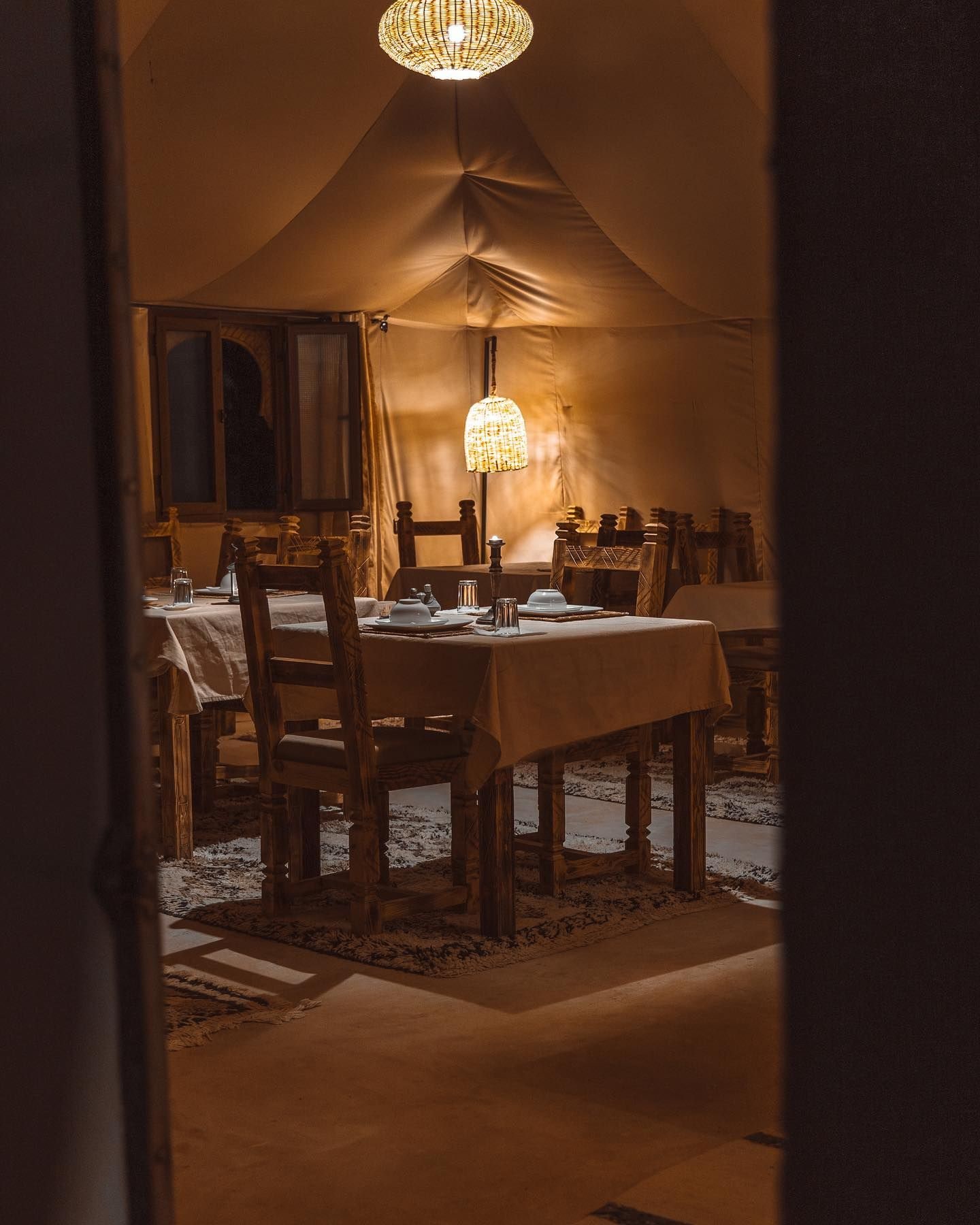 Área de refeições coberta com tenda, mesa posta para dois, cadeiras de madeira, um lustre e vista para a paisagem nevada.
