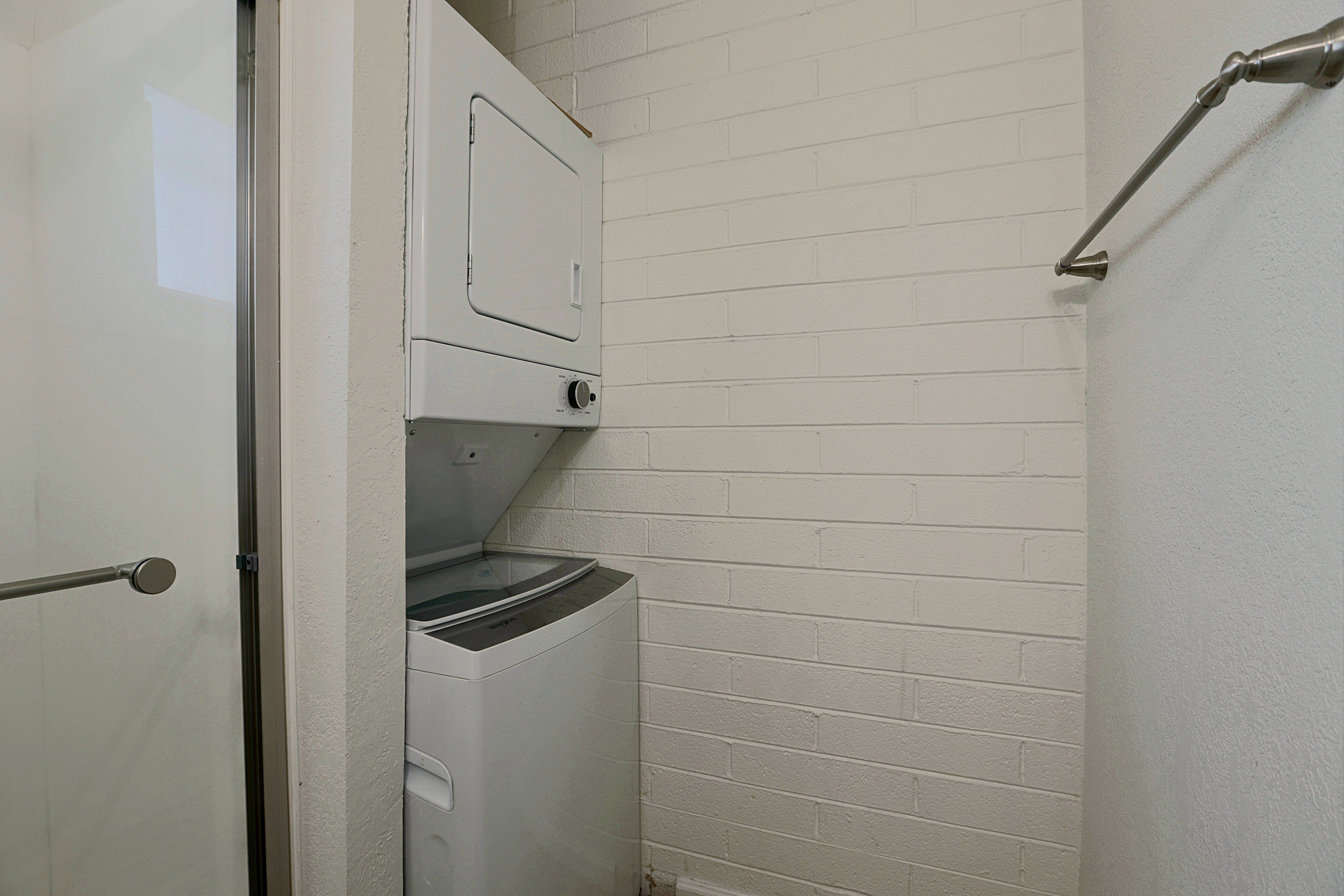 Uma lavanderia com máquina de lavar e secadora, uma porta e uma parede de tijolos.