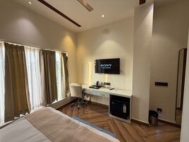 Quarto de hotel com cama, escrivaninha com televisão, cadeira e pequeno frigorífico.