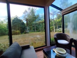 Quarto com uma janela grande, uma cadeira de vime, um sofá e uma mesa com uma tigela.