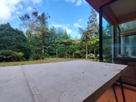 Quarto com uma grande janela com vista para um jardim com várias árvores e arbustos.
