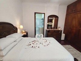 Quarto de hotel com cama, mesa de cabeceira com abajur, cômoda, espelho e guarda-roupa.
