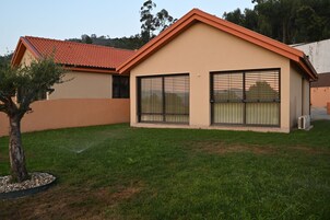 Um edifício térreo com telhado inclinado, grandes janelas e uma pequena árvore ao primeiro plano.