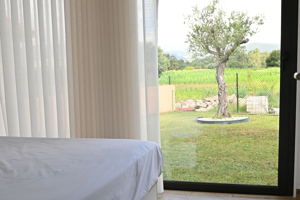 Quarto com cama, vista de um jardim por uma porta aberta e janela com cortinas.