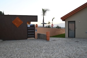 Uma entrada com portão e detector de metal, uma palmeira e um edifício com telhado vermelho.