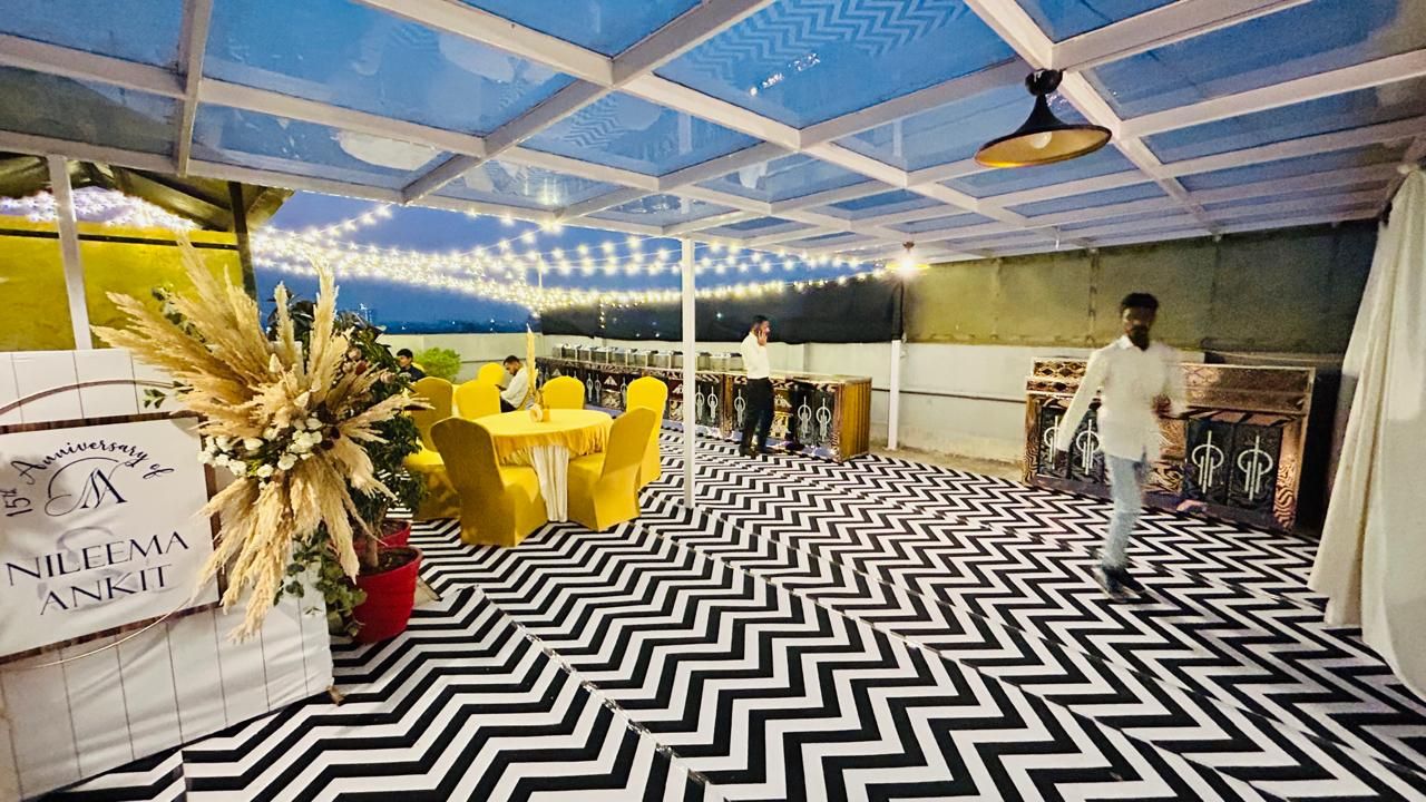 Terraço no telhado com piso estampado, cadeiras amarelas, uma mesa e uma planta decorativa.