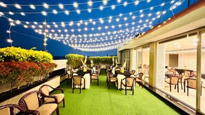 Uma área de refeições ao ar livre com luzes de festa, grama sintética verde e assentos externos.