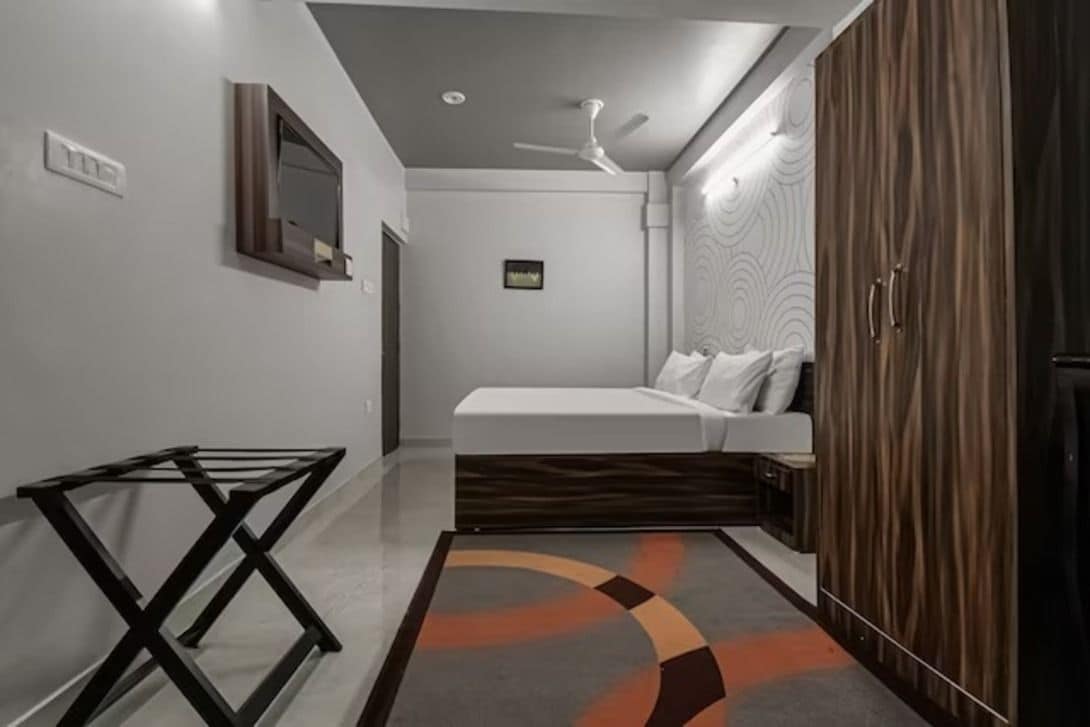 Quarto com cama, guarda-roupa, ventoinha no teto e uma pequena mesa.