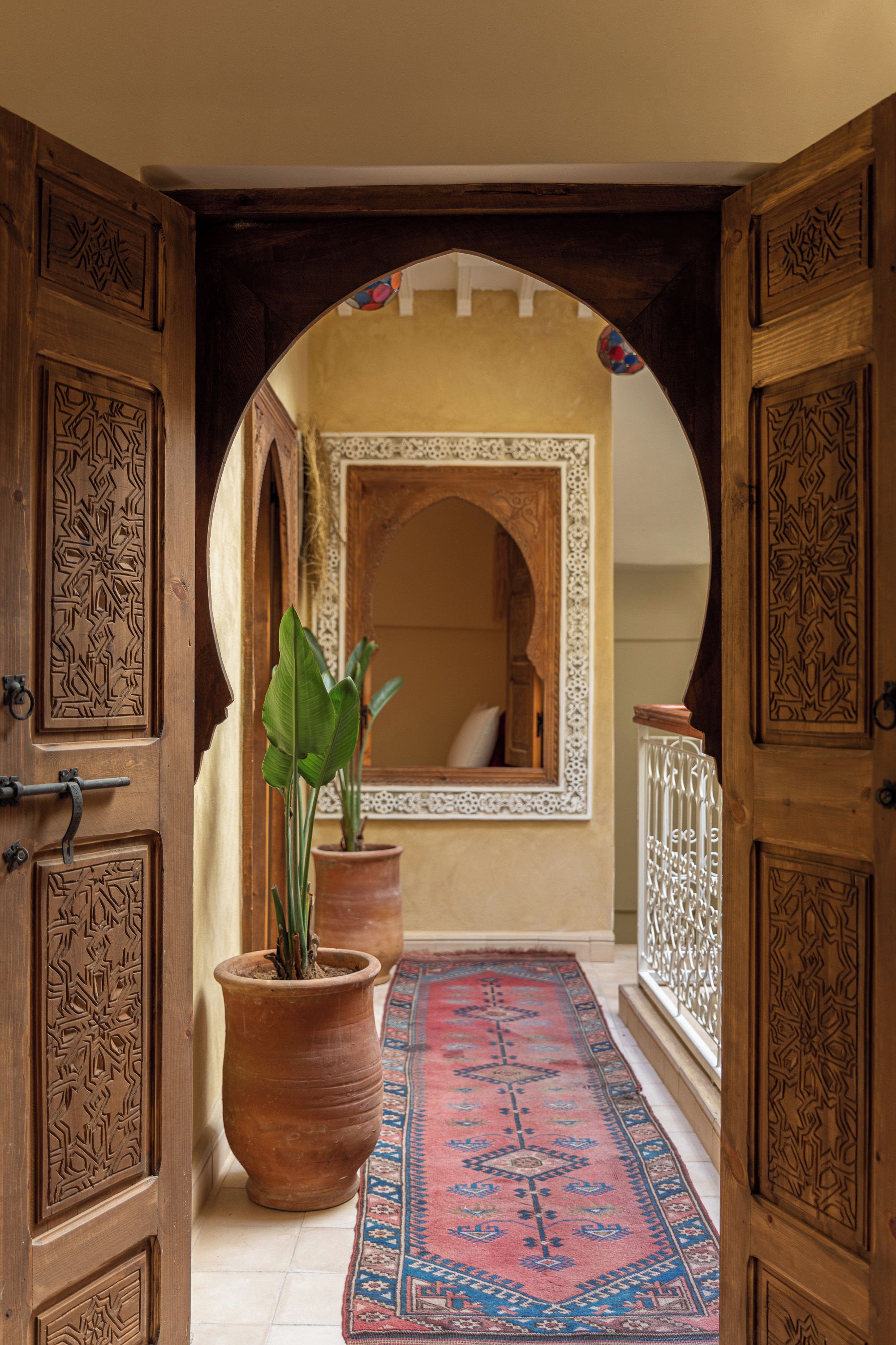 Corredor interno com portas de madeira, um vaso de planta e um tapete estampado.