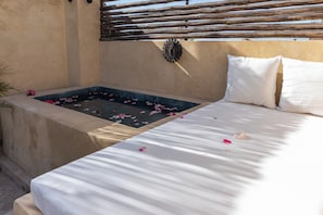 Quarto com uma cama, uma banheira pequena com pétalas de rosa e um cercado de madeira.