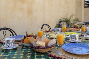 Mesa posta com itens de café da manhã, incluindo pão, frutas e suco de laranja.