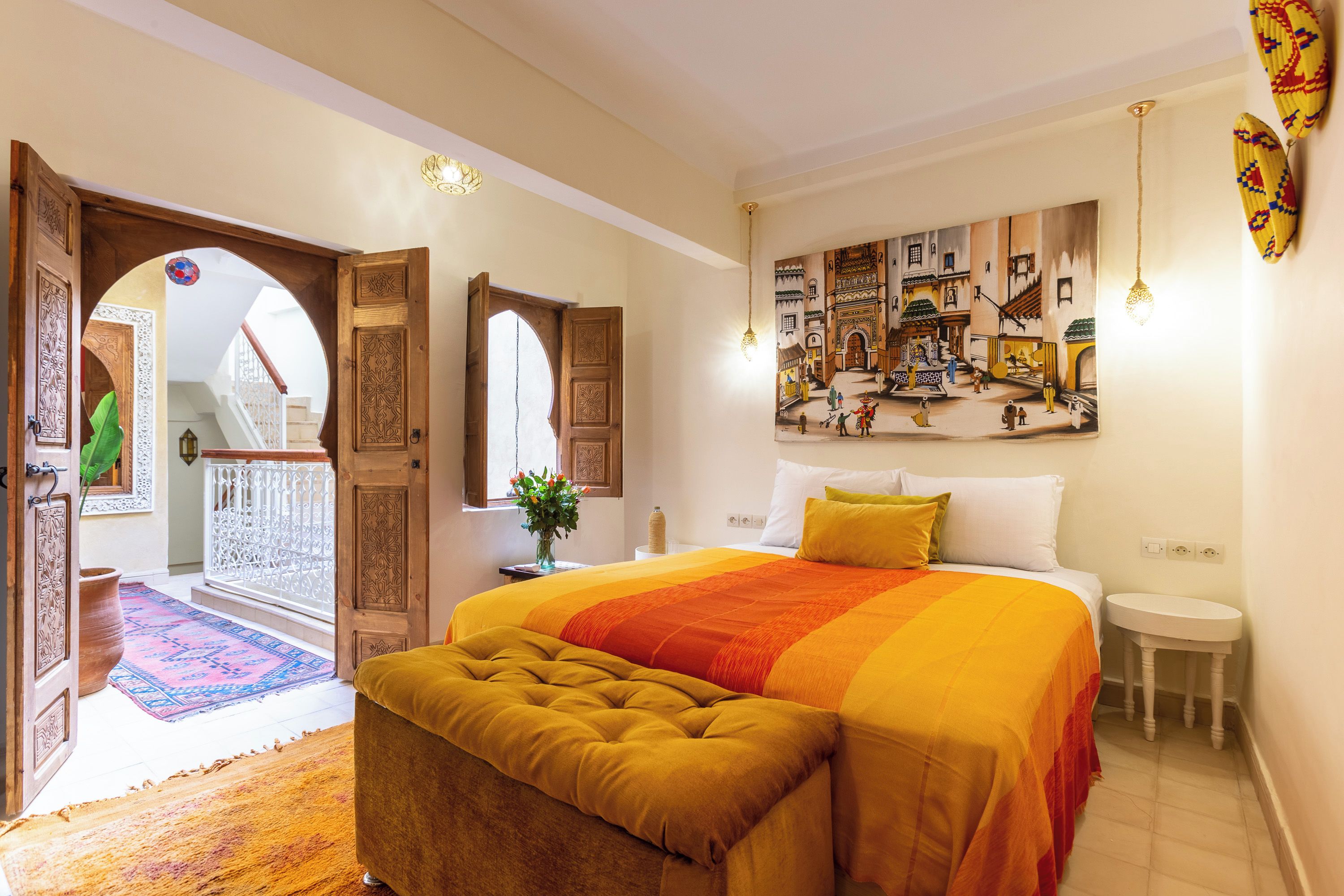 Quarto com cama grande, um banquinho, uma pintura e vista para um pátio.