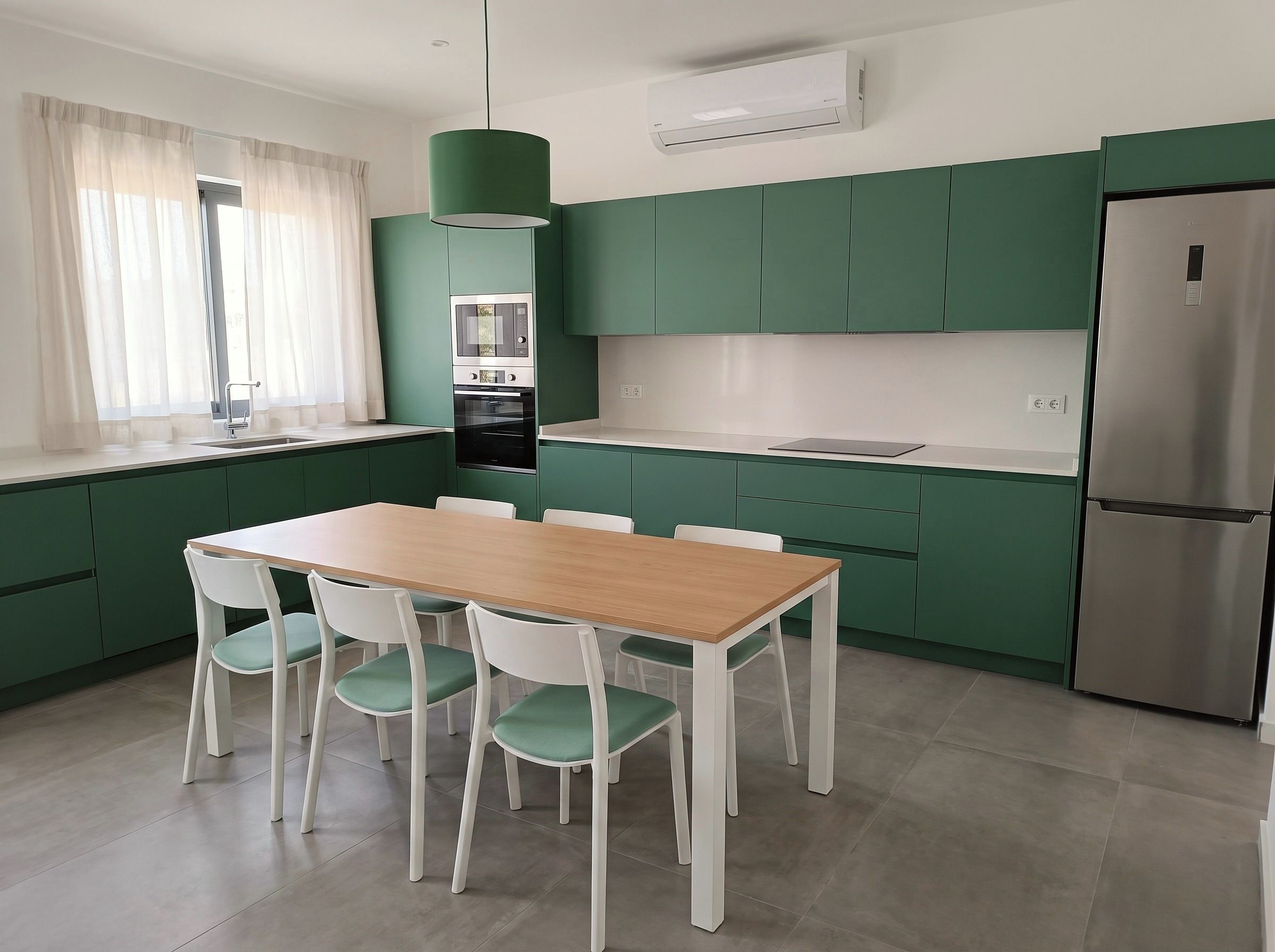 Cozinha moderna com armários verdes, geladeira de aço inoxidável, forno embutido e mesa de jantar com cadeiras.