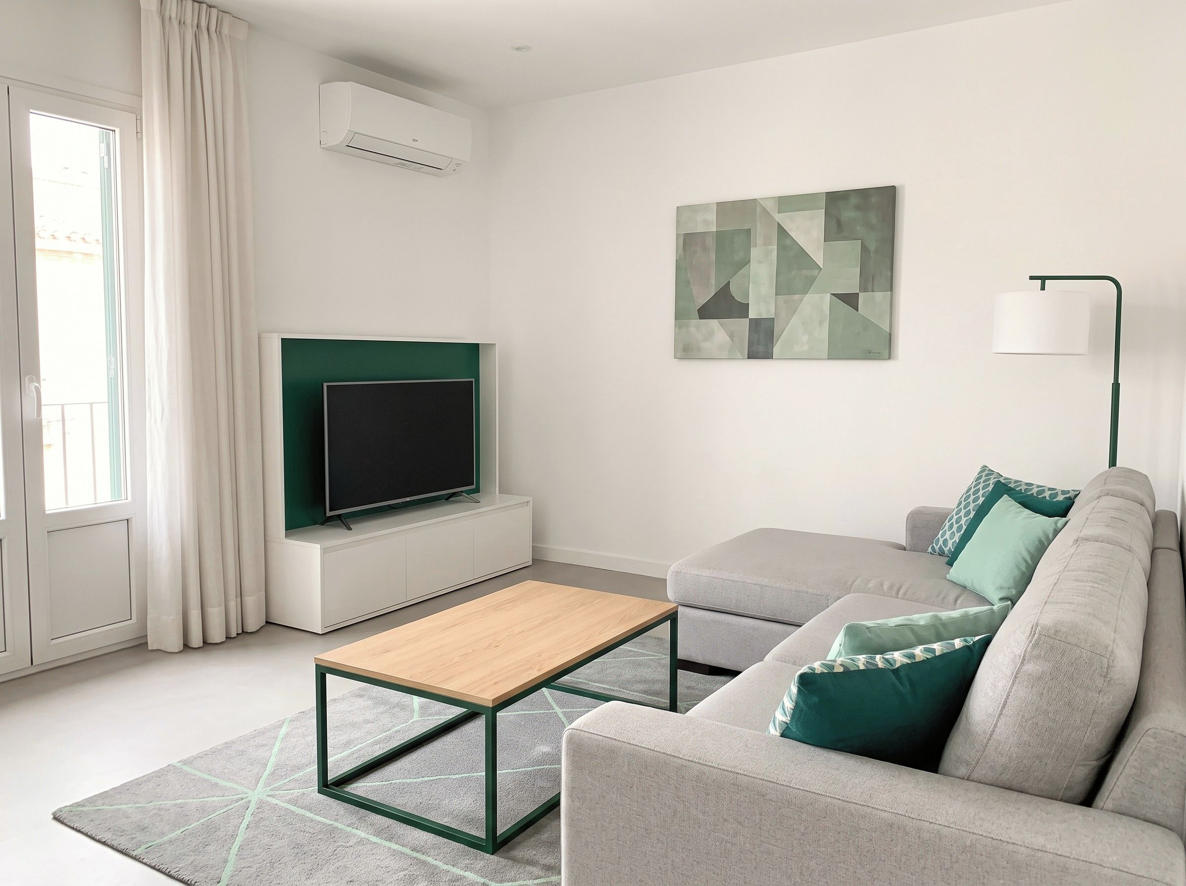 Uma sala de estar moderna com televisão de tela plana, sofá, mesa de centro e um quadro na parede.