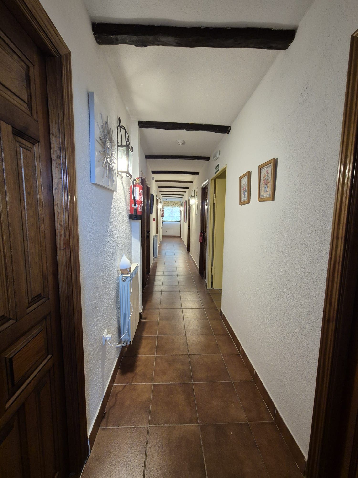 Um corredor com piso de azulejos, portas de madeira e um extintor de incêndio na parede.