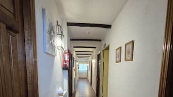 Um corredor com piso de azulejos, portas de madeira e um extintor de incêndio na parede.