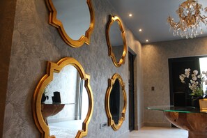 Quarto com quatro grandes espelhos dourados na parede, uma mesa de centro de vidro e um candelabro.