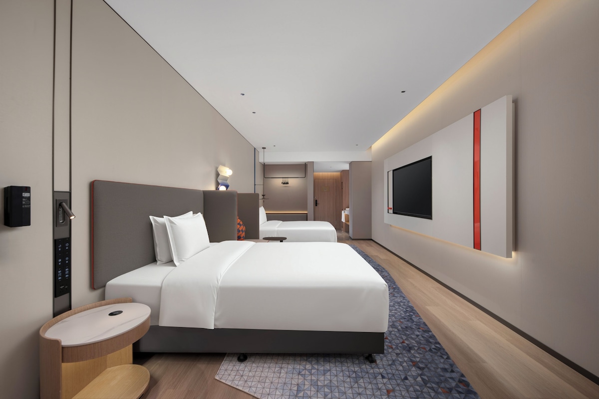 Quarto de hotel moderno com uma cama grande, mesas de cabeceira, televisão e banheiro visível por uma porta aberta.