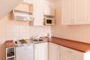 Cozinha compacta com armários brancos, pia de aço inoxidável, micro-ondas e chaleira.