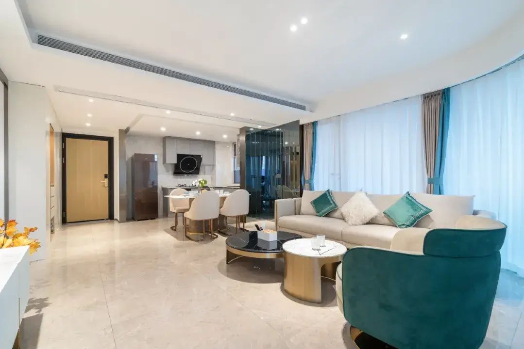 Uma sala de estar moderna com sofá, mesa de centro e cadeiras, uma área de jantar com mesa e cadeiras, e uma cozinha ao fundo.
