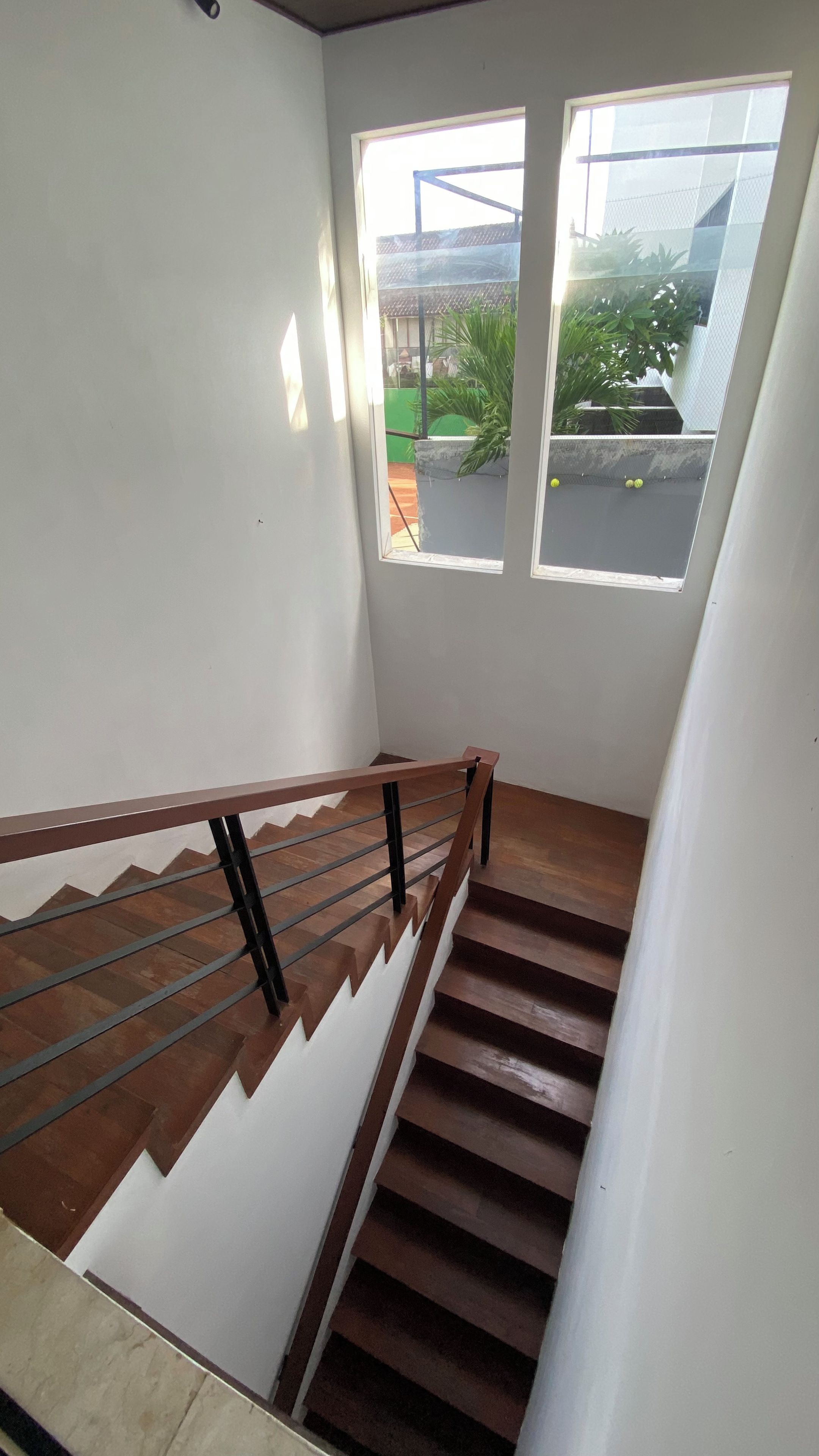 Escadaria com degraus de madeira e corrimãos de metal, que leva a um patamar com vista para uma área externa arborizada.