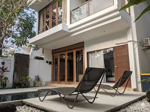 Uma casa moderna de dois andares com varanda, piscina e duas cadeiras de descanso.