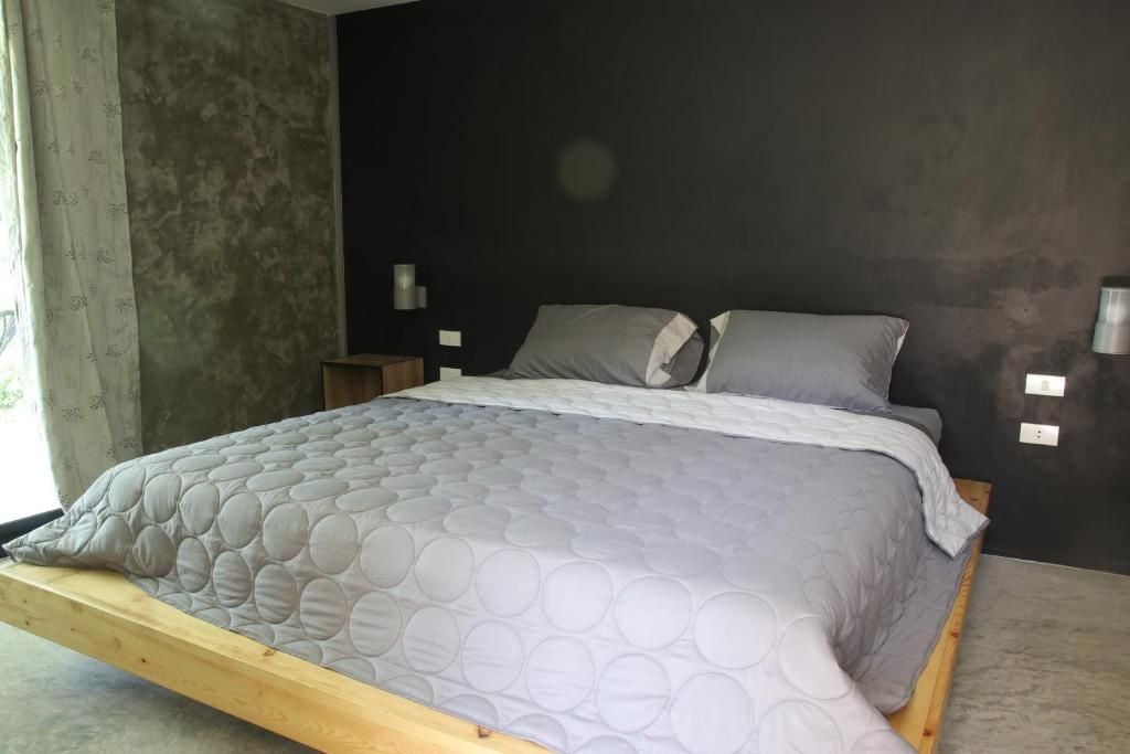 Uma cama de solteiro com um edredom cinzento num quarto com parede escura e janela com cortinas.